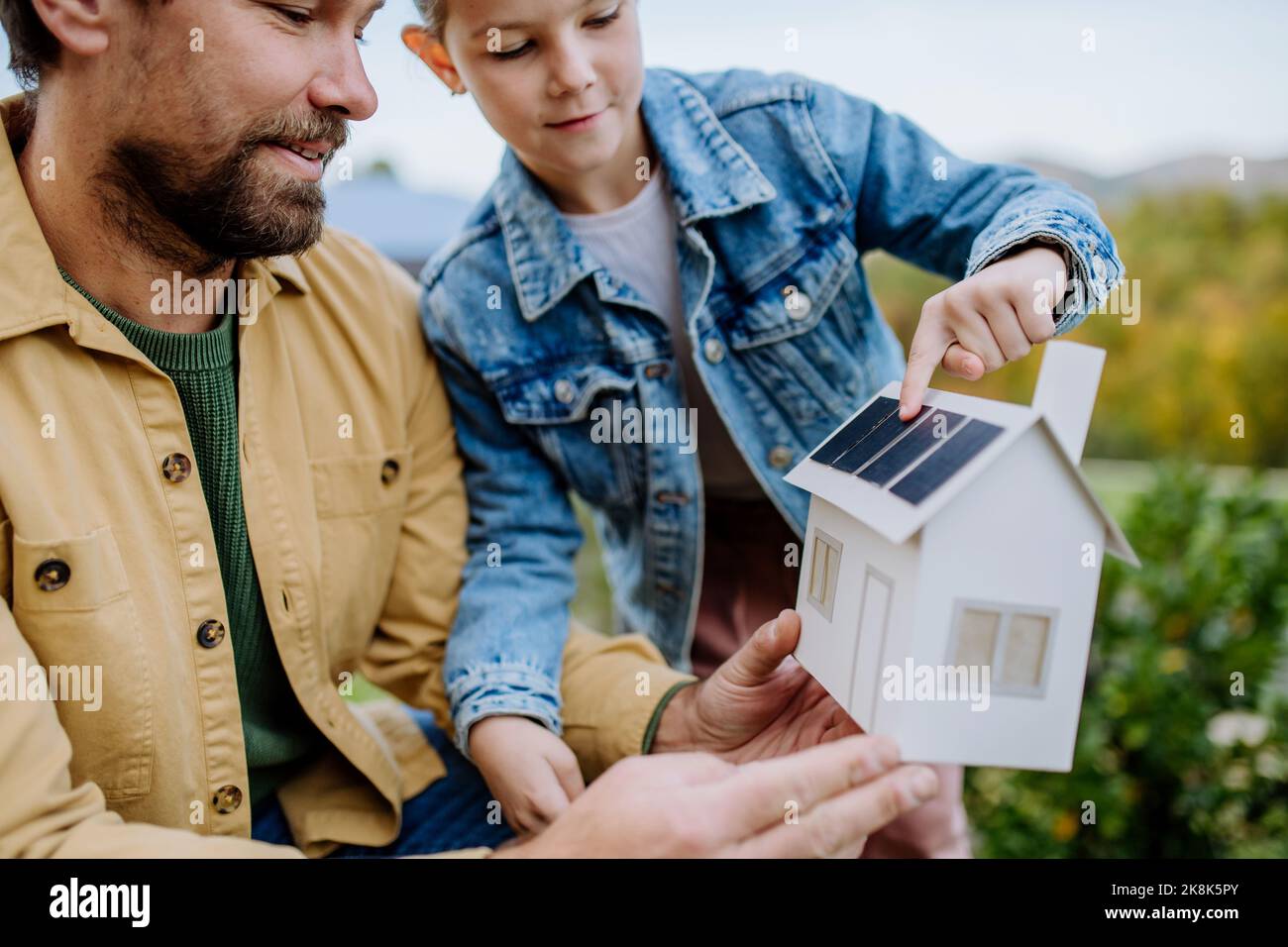 Little girl with her dad holding paper model of house with solar panels ...