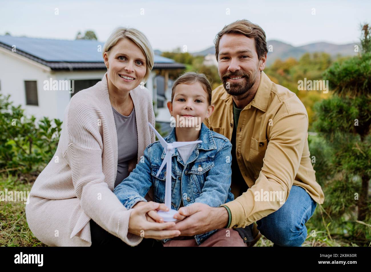 Happy family holding plastic model of wind turbine. Alternative energy ...
