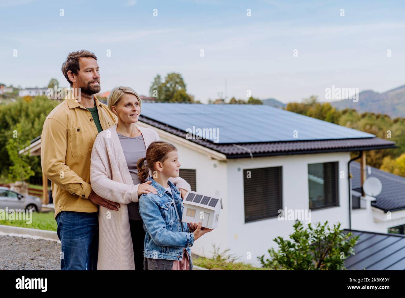 Happy family holding paper model of house with solar panels.Alternative ...