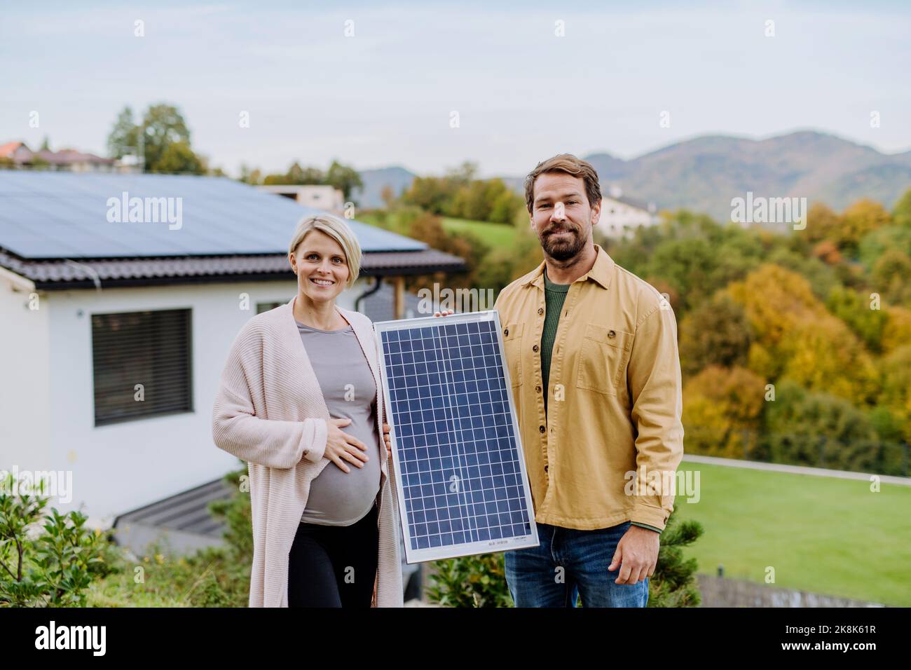 Happy couple standying near their house with solar panels. Alternative ...