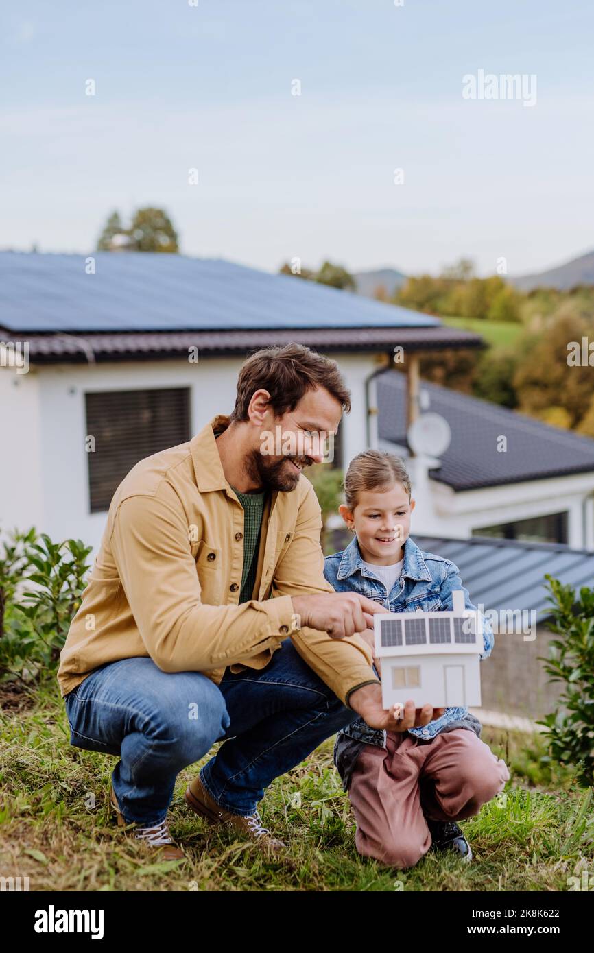 Little girl with her dad holding paper model of house with solar panels ...