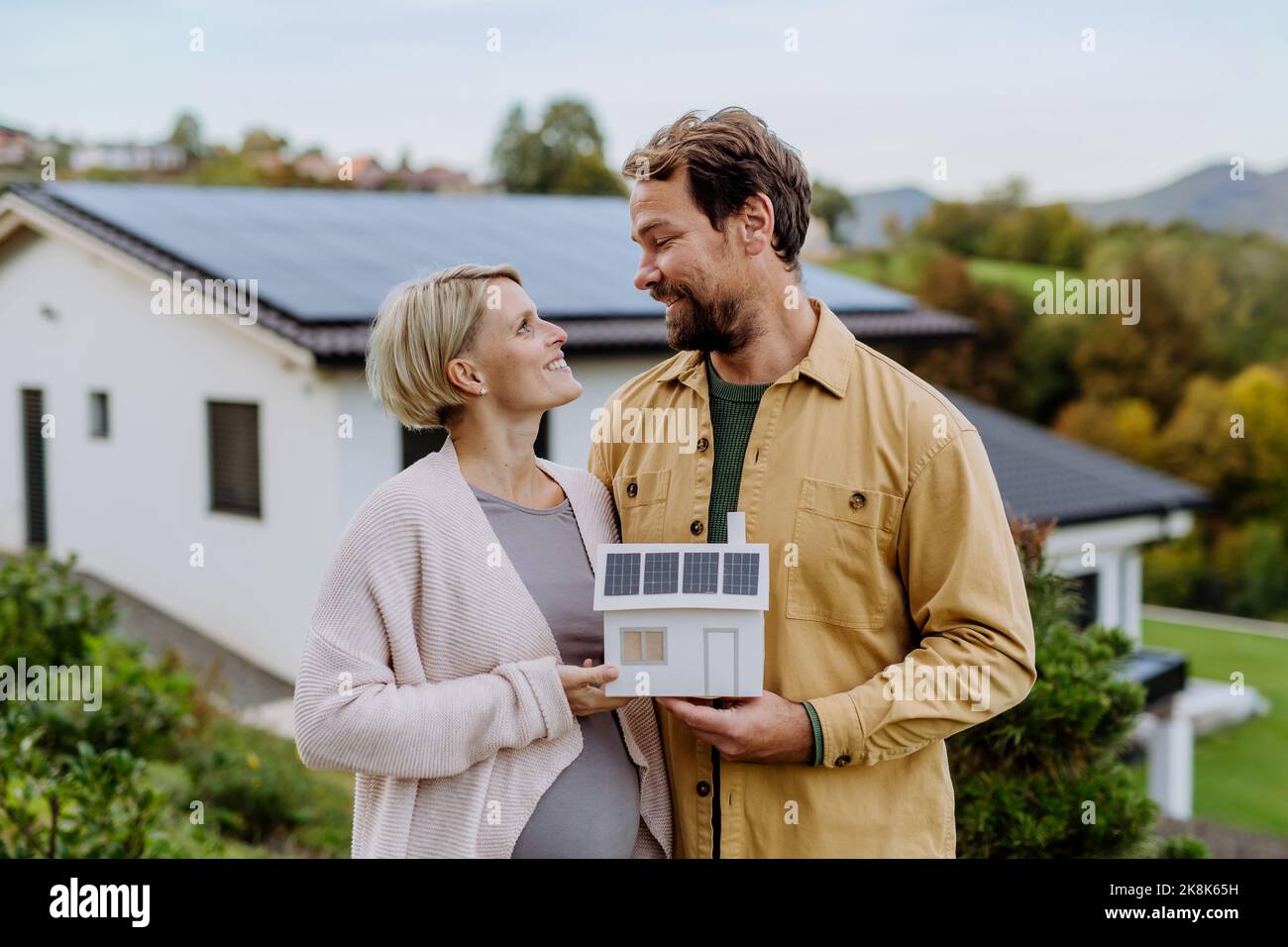 Close up of happy couple holding paper model of house with solar panels ...