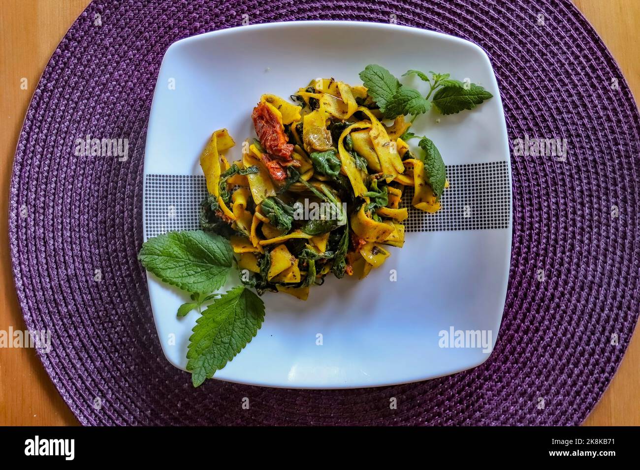 A delicious plate of pasta with different green spices on a purple ...