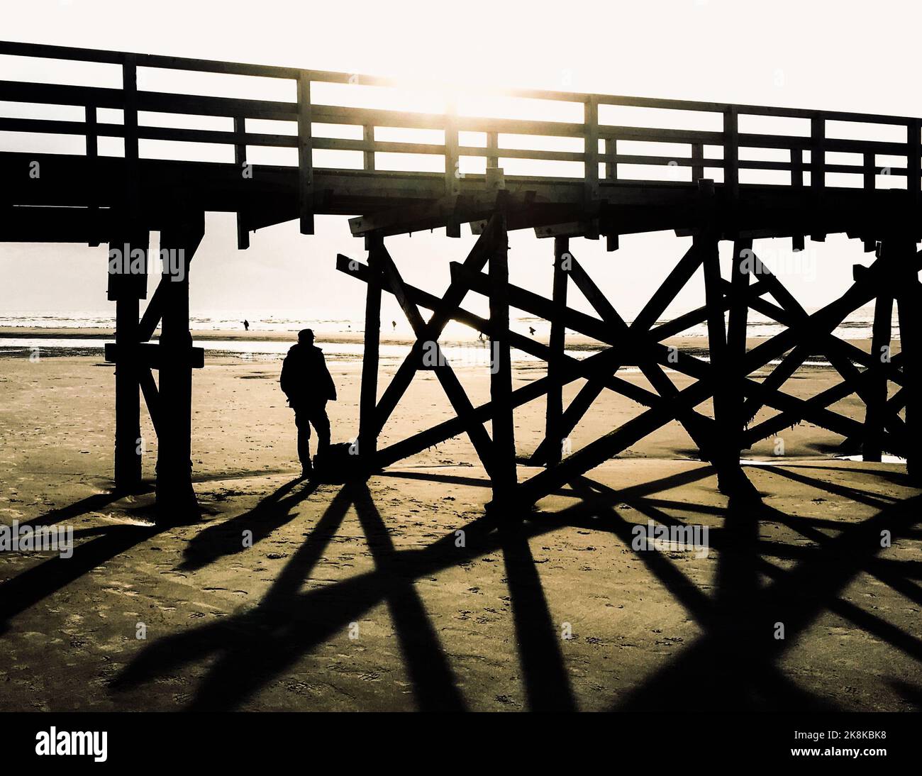 A man under a wooden bridge by the beach at sunrise with light and ...