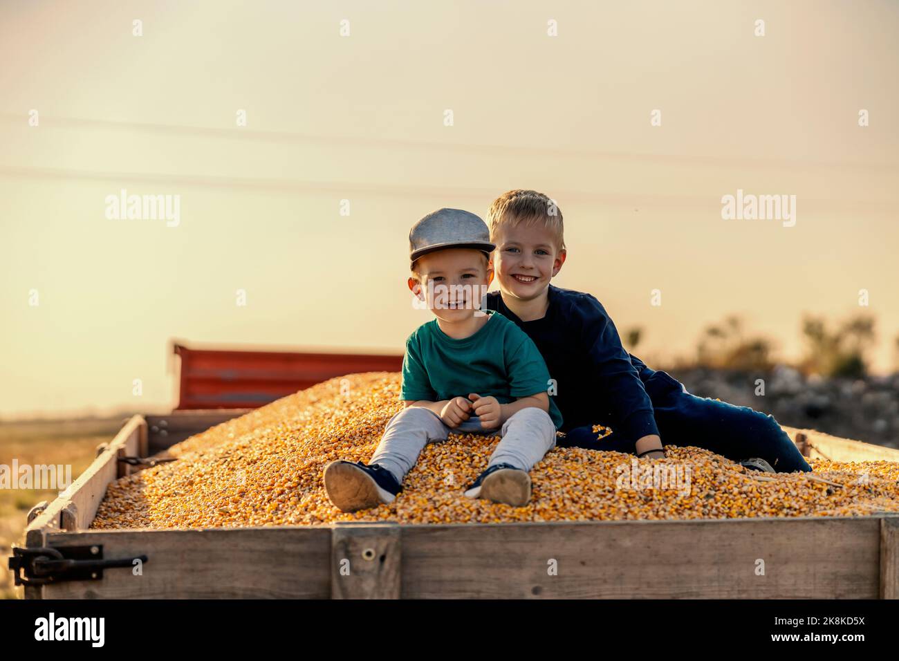 Two little farmer boys are sitting on the pile of corn grains in a ...