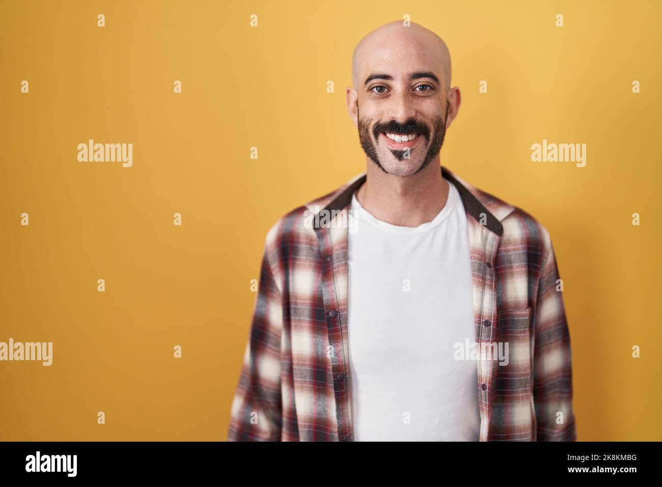 Hispanic man with beard standing over yellow background with a happy ...