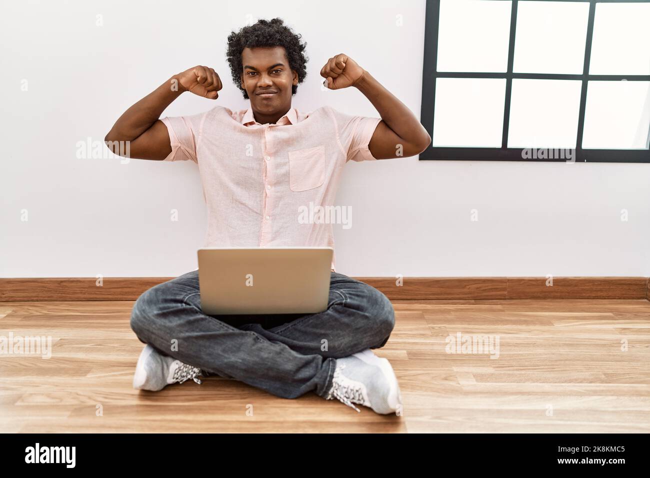 African man with curly hair using laptop sitting on the floor showing ...
