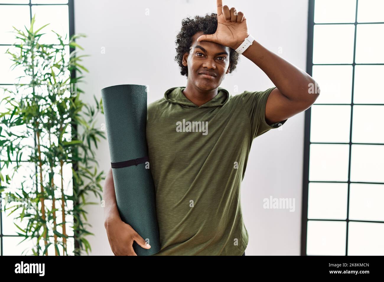 African man with curly hair holding yoga mat at studio making fun of ...