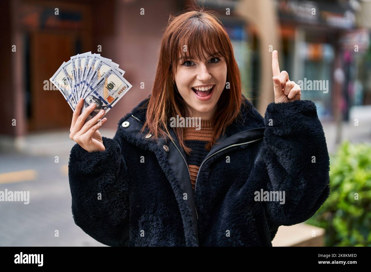 Young beautiful woman holding dollars banknotes smiling with an idea or ...