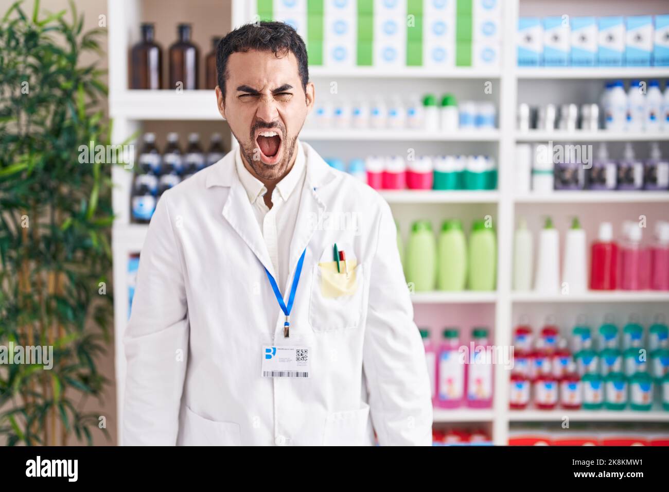Handsome hispanic man working at pharmacy drugstore angry and mad ...