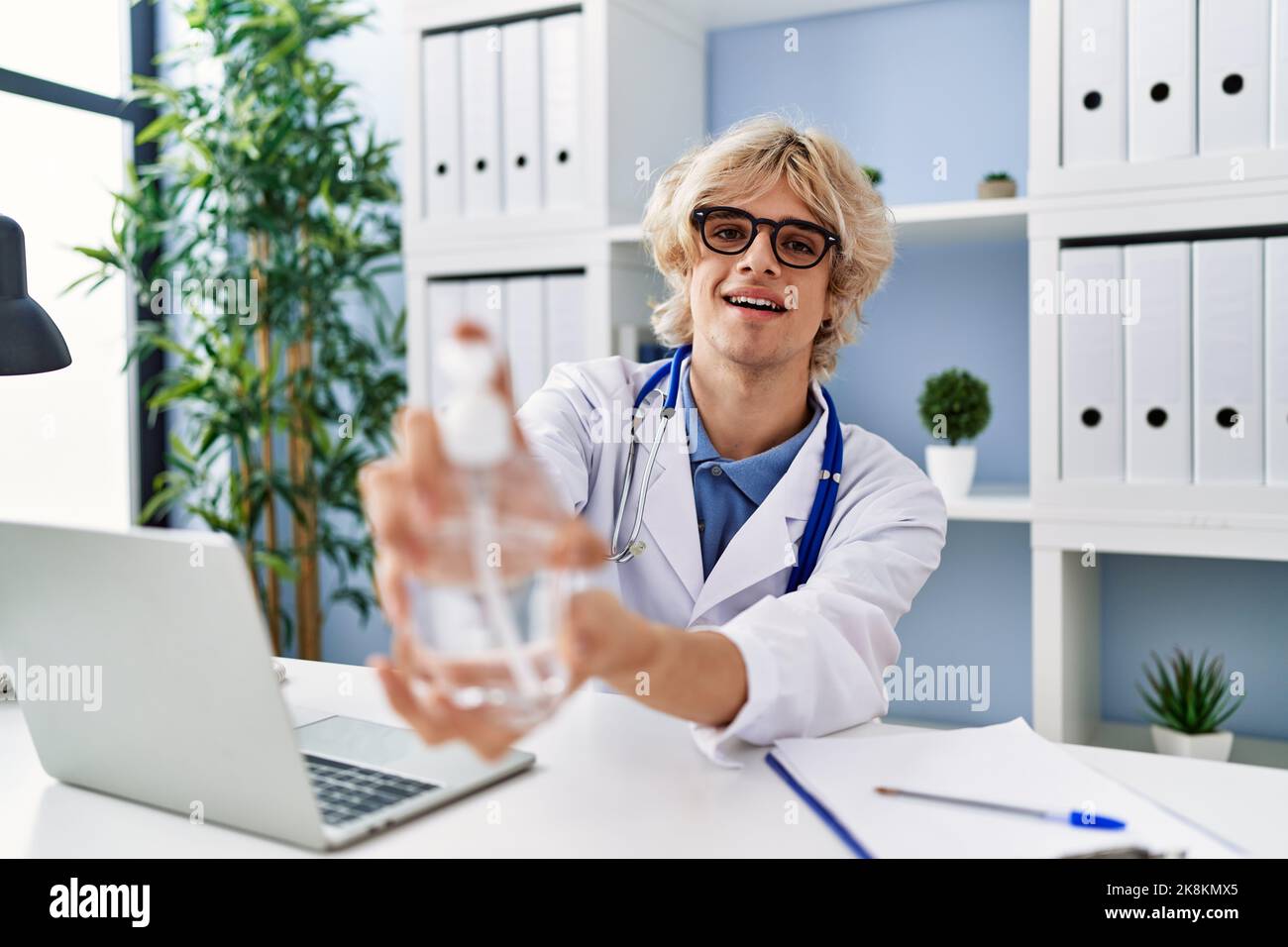 Young blond man doctor smiling confident using sanitizer gel hands at ...