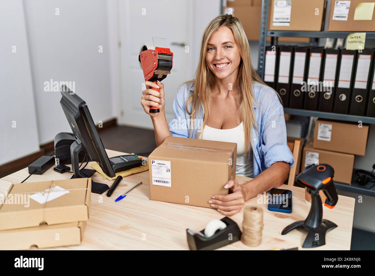 Young blonde woman ecommerce business worker holding packing tape ...