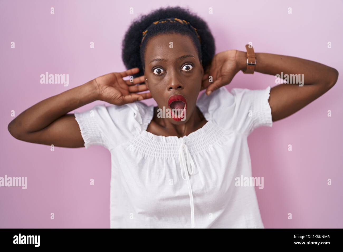 African woman with curly hair standing over pink background crazy and ...