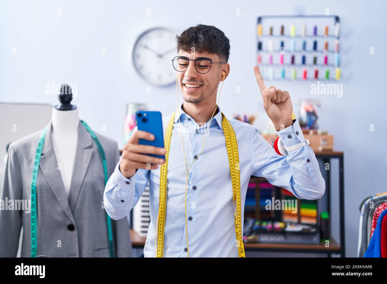 Young hispanic man dressmaker designer using smartphone smiling with an ...