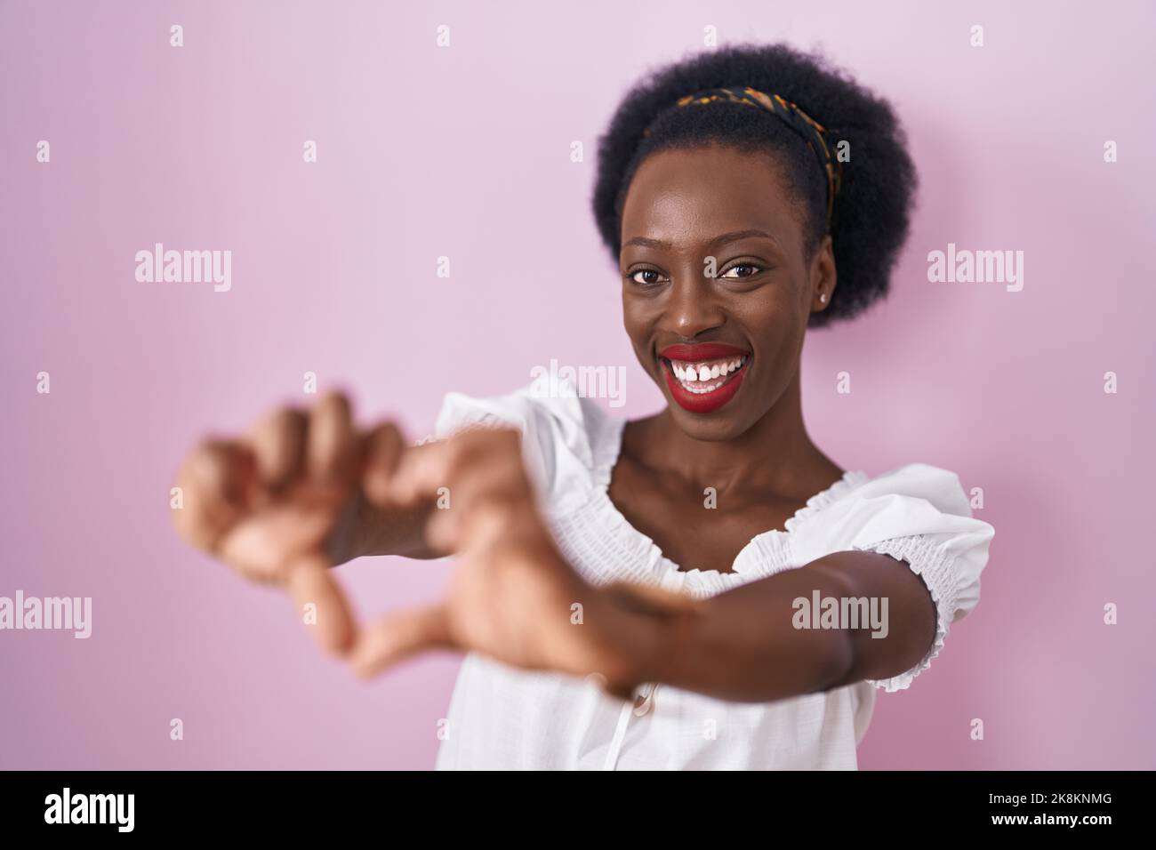 African woman with curly hair standing over pink background smiling in ...