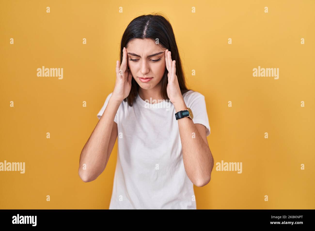 Young beautiful woman standing over yellow background with hand on head ...