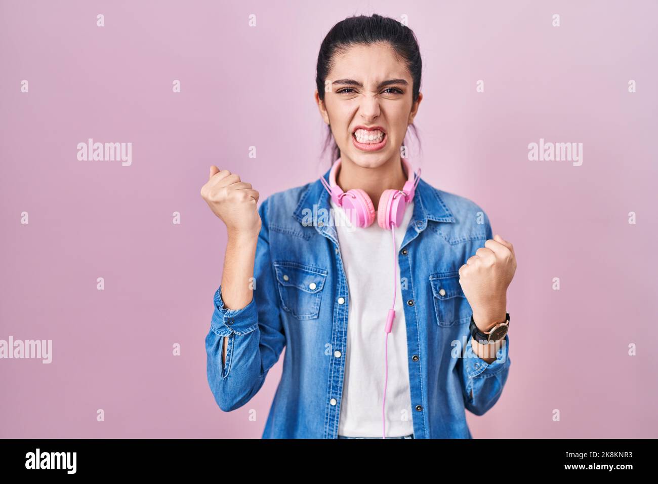Young beautiful woman standing over pink background angry and mad ...