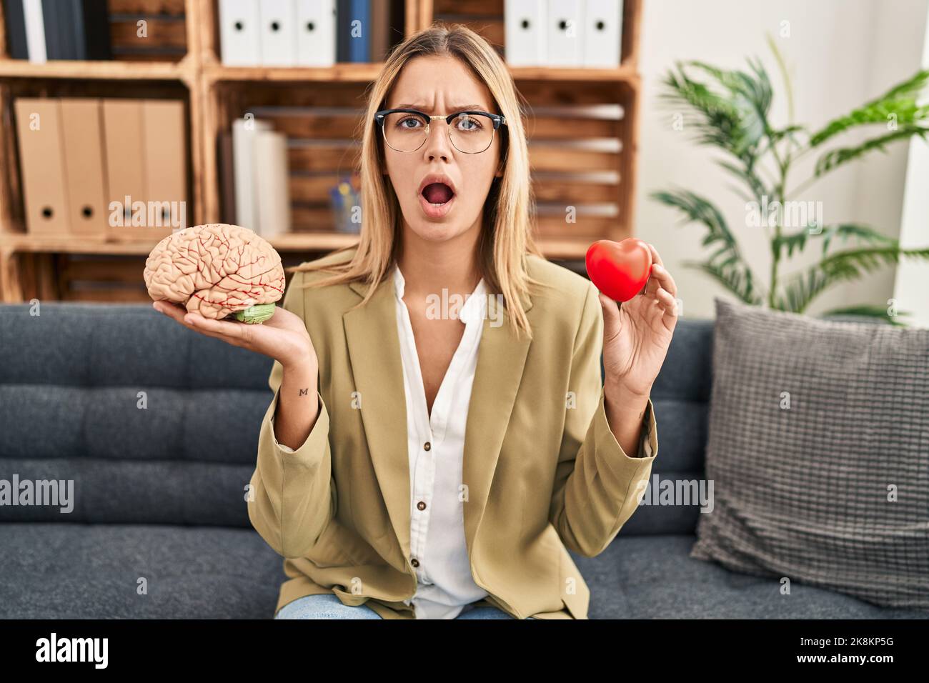 Young blonde woman working at therapy office holding brain and health ...