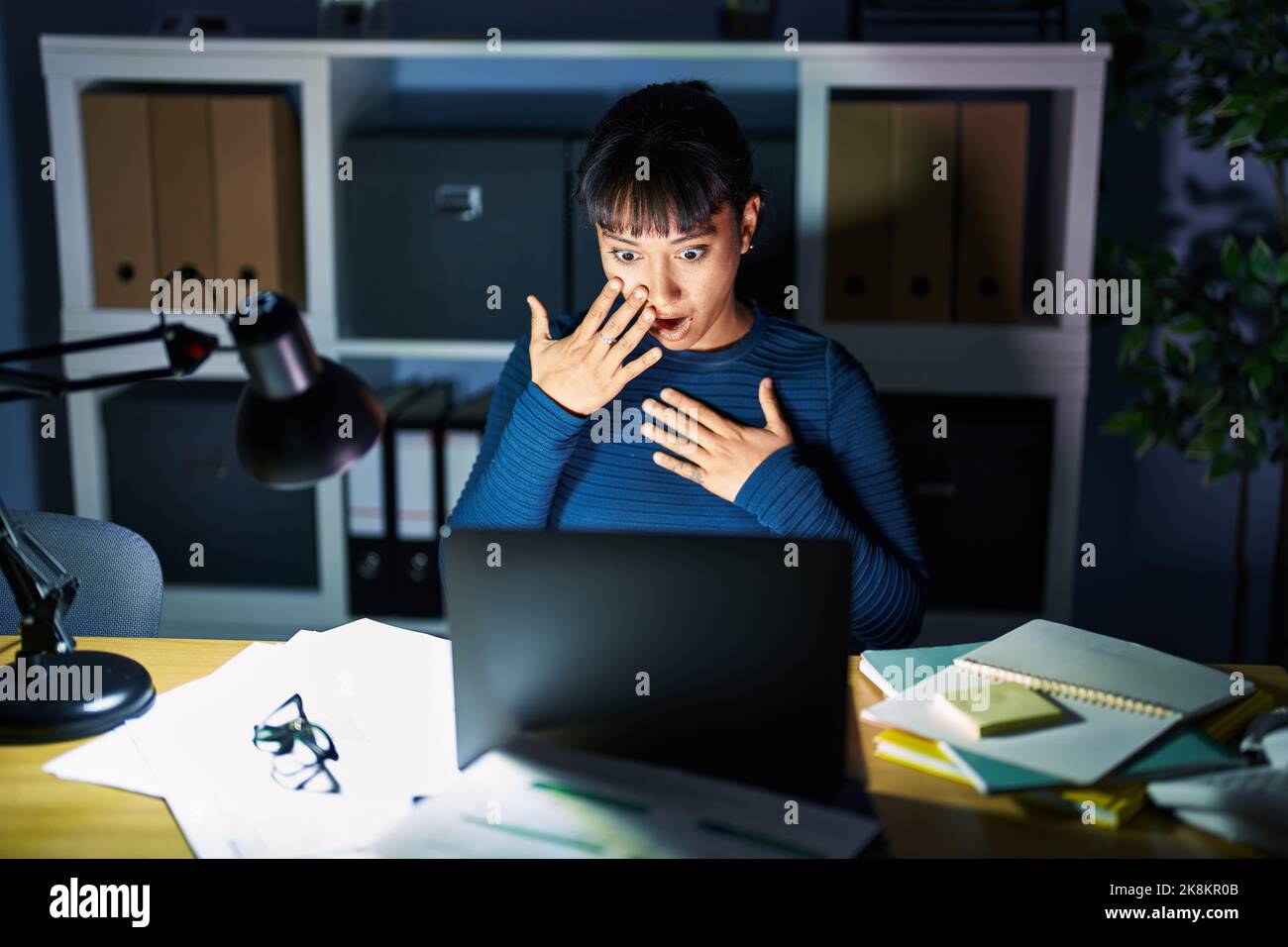 Young beautiful woman working at the office at night afraid and ...
