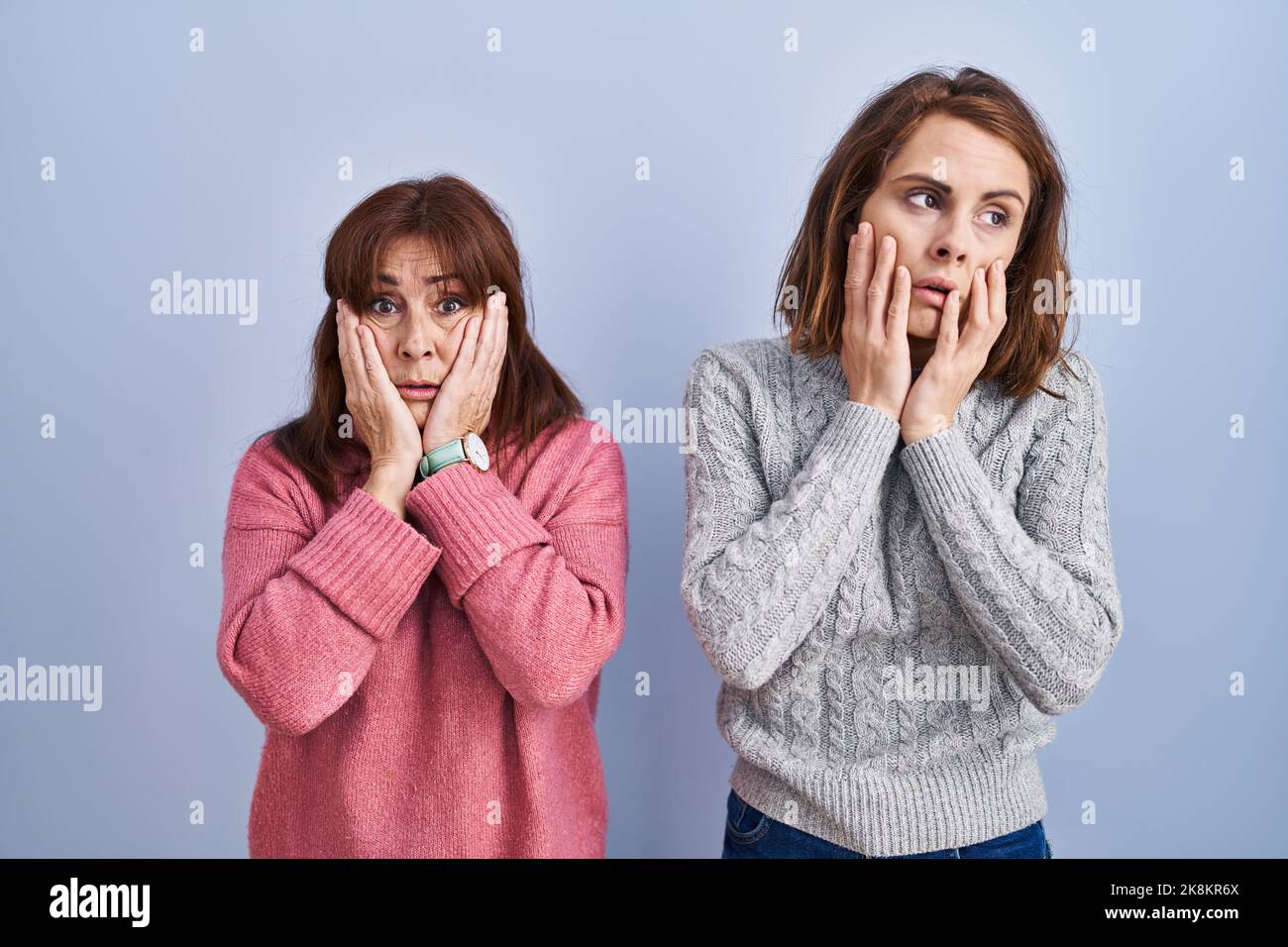 Mother and daughter standing over blue background tired hands covering ...