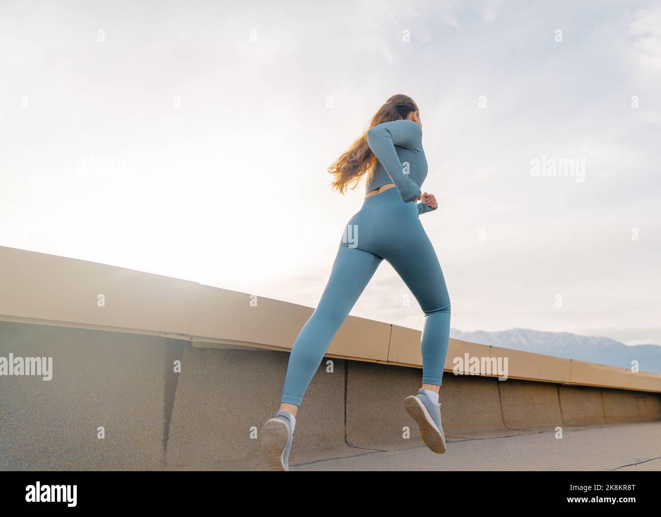 Athletic woman is running on rooftop of parking, garage on sunset ...