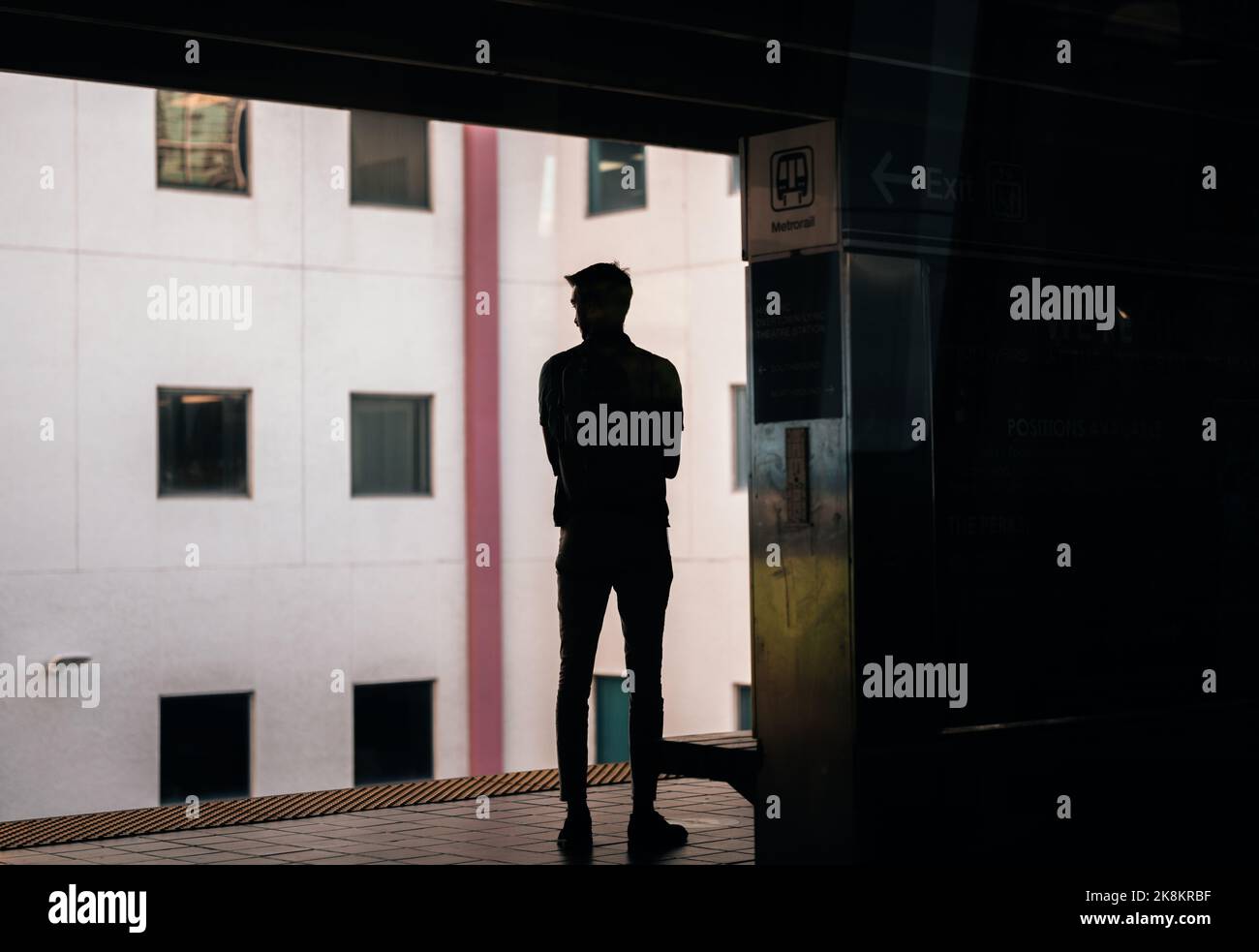 A man standing backside next to a metrorail sign in a dark place ...