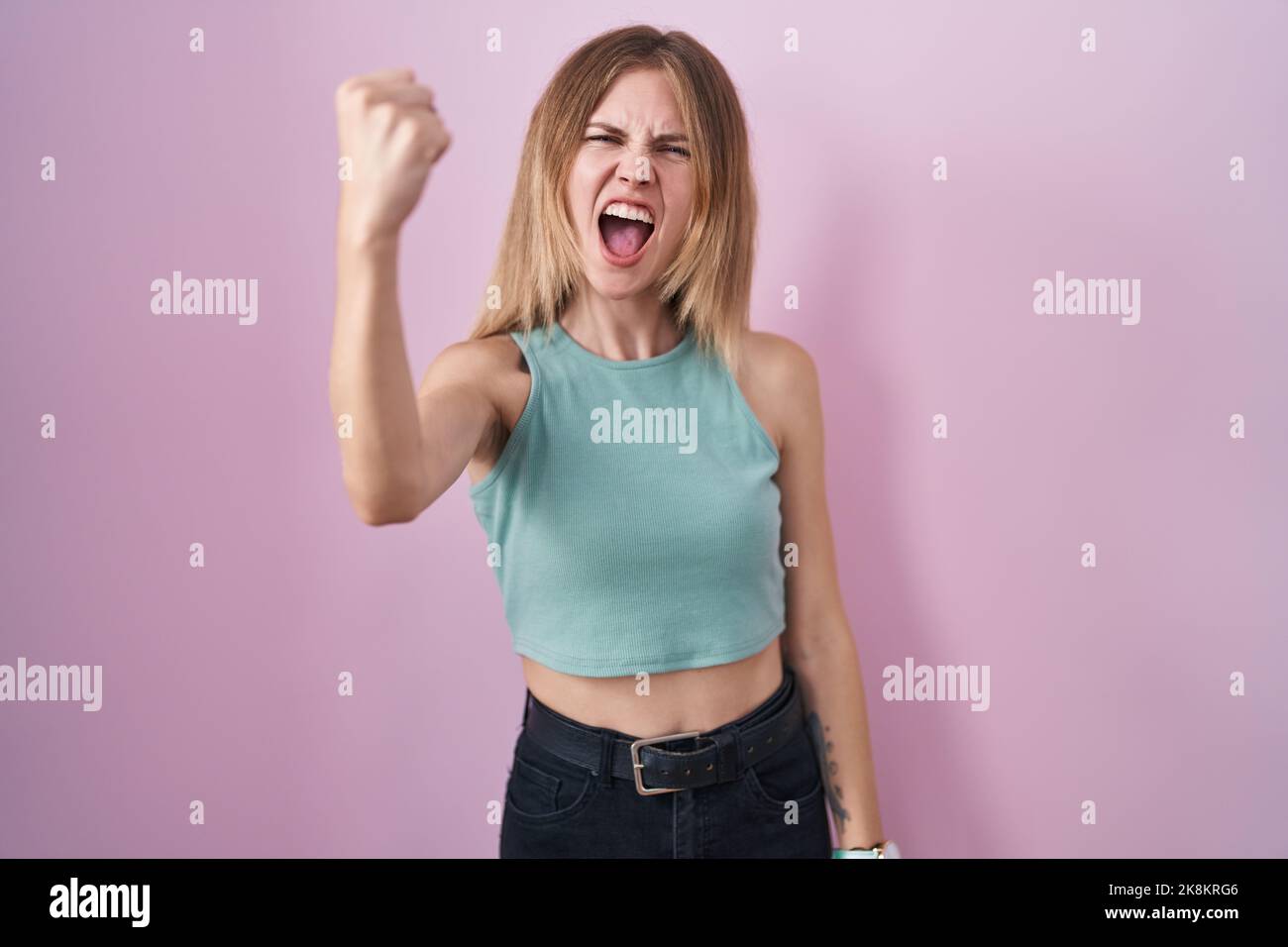 Blonde caucasian woman standing over pink background angry and mad ...