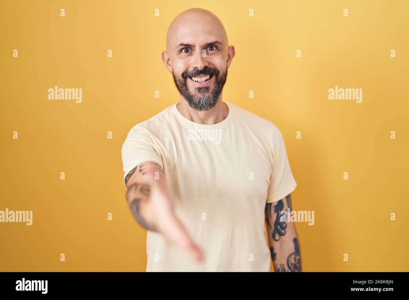 Hispanic man with tattoos standing over yellow background smiling ...