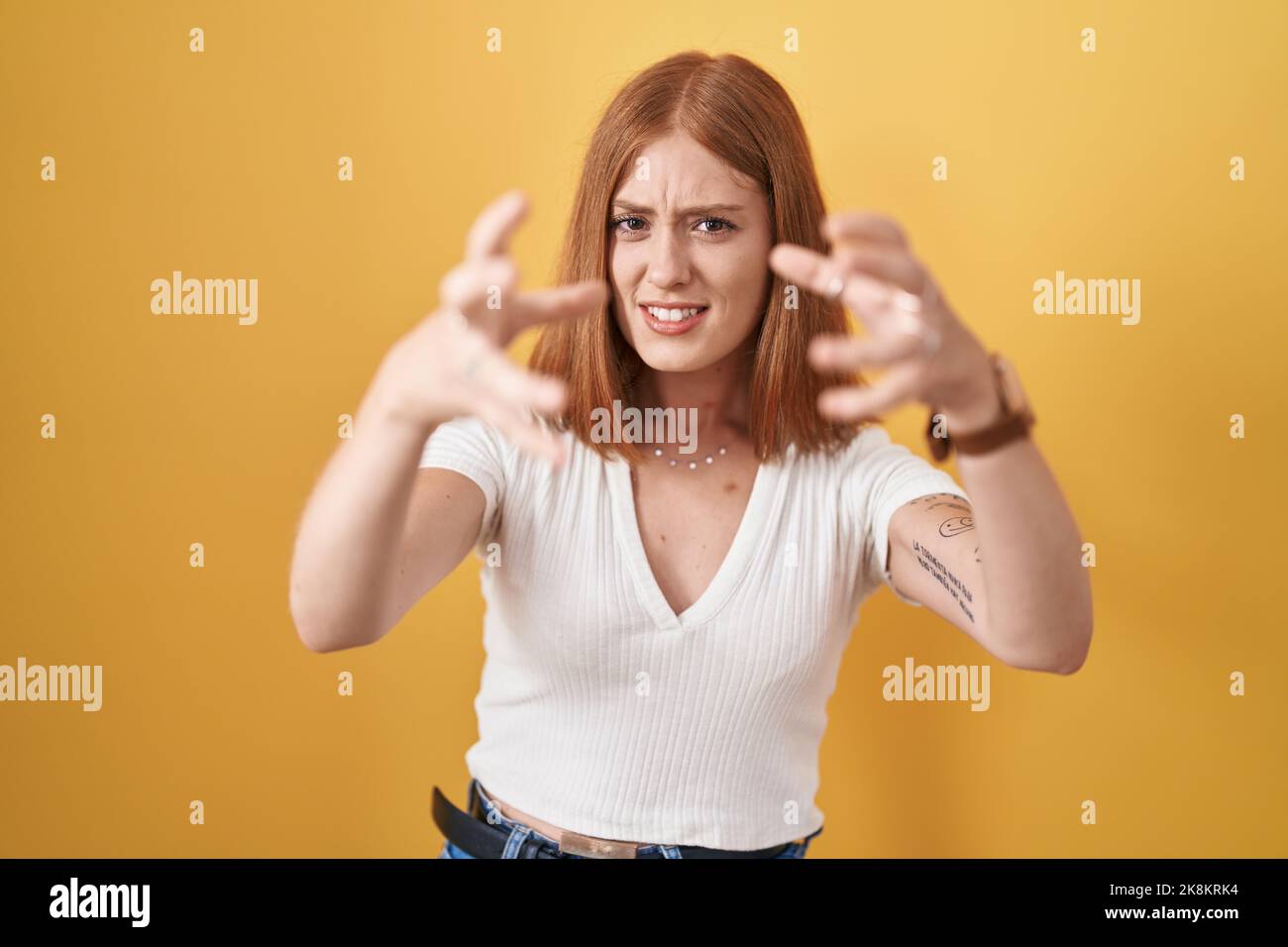 Young redhead woman standing over yellow background shouting frustrated ...