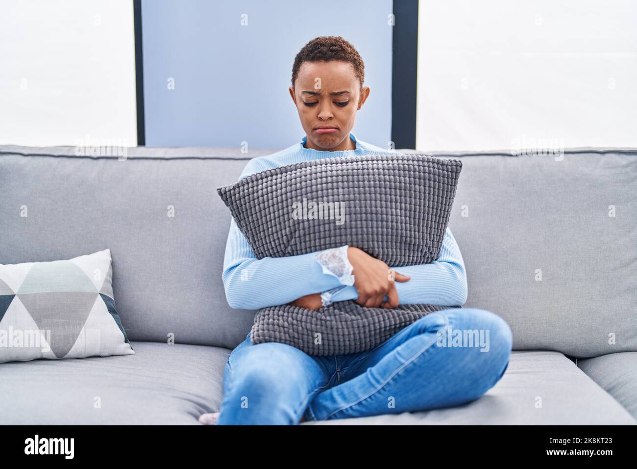 African american woman sitting on the sofa at home hugging pillow ...