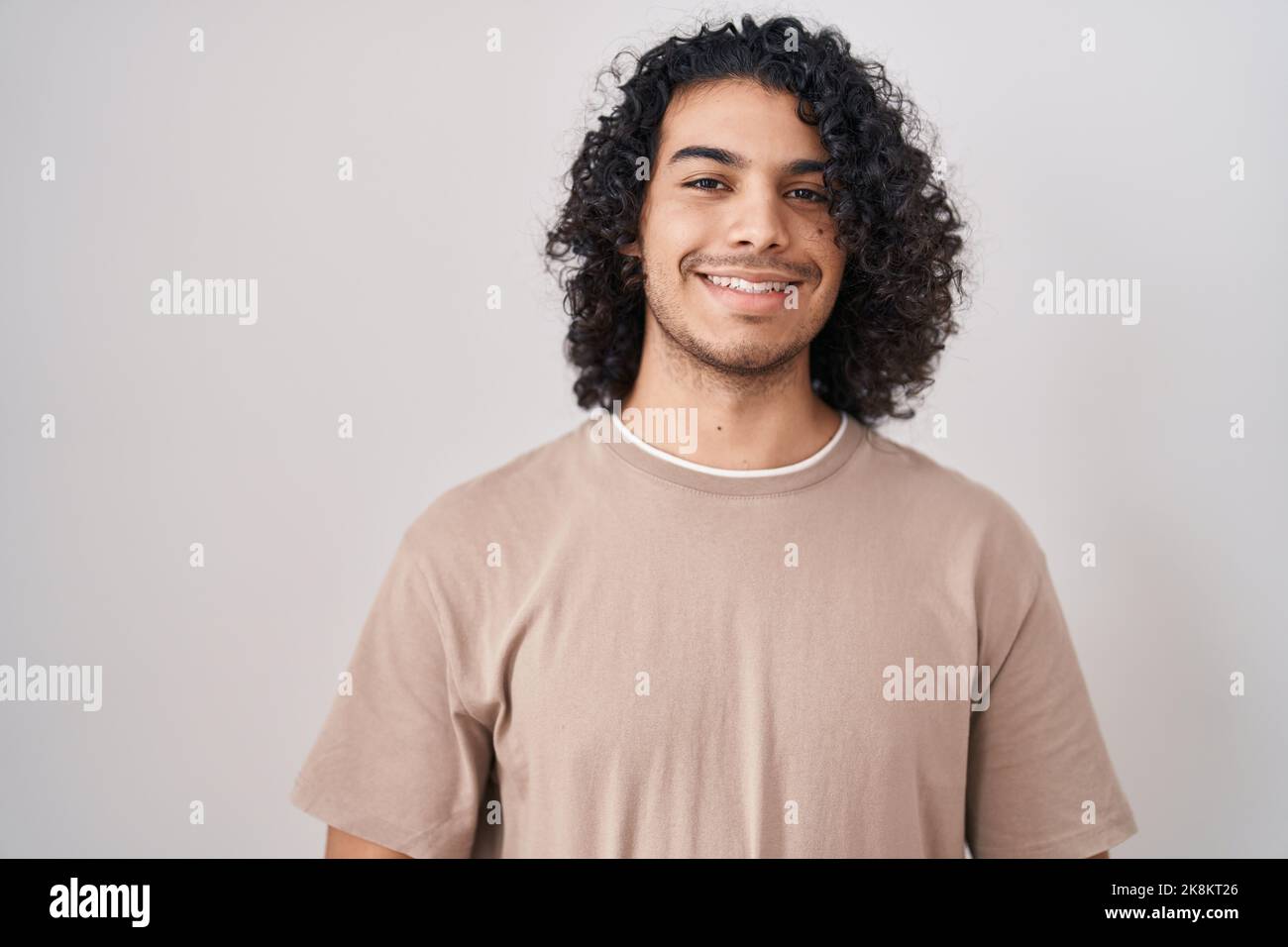 Hispanic man with curly hair standing over white background with hands ...