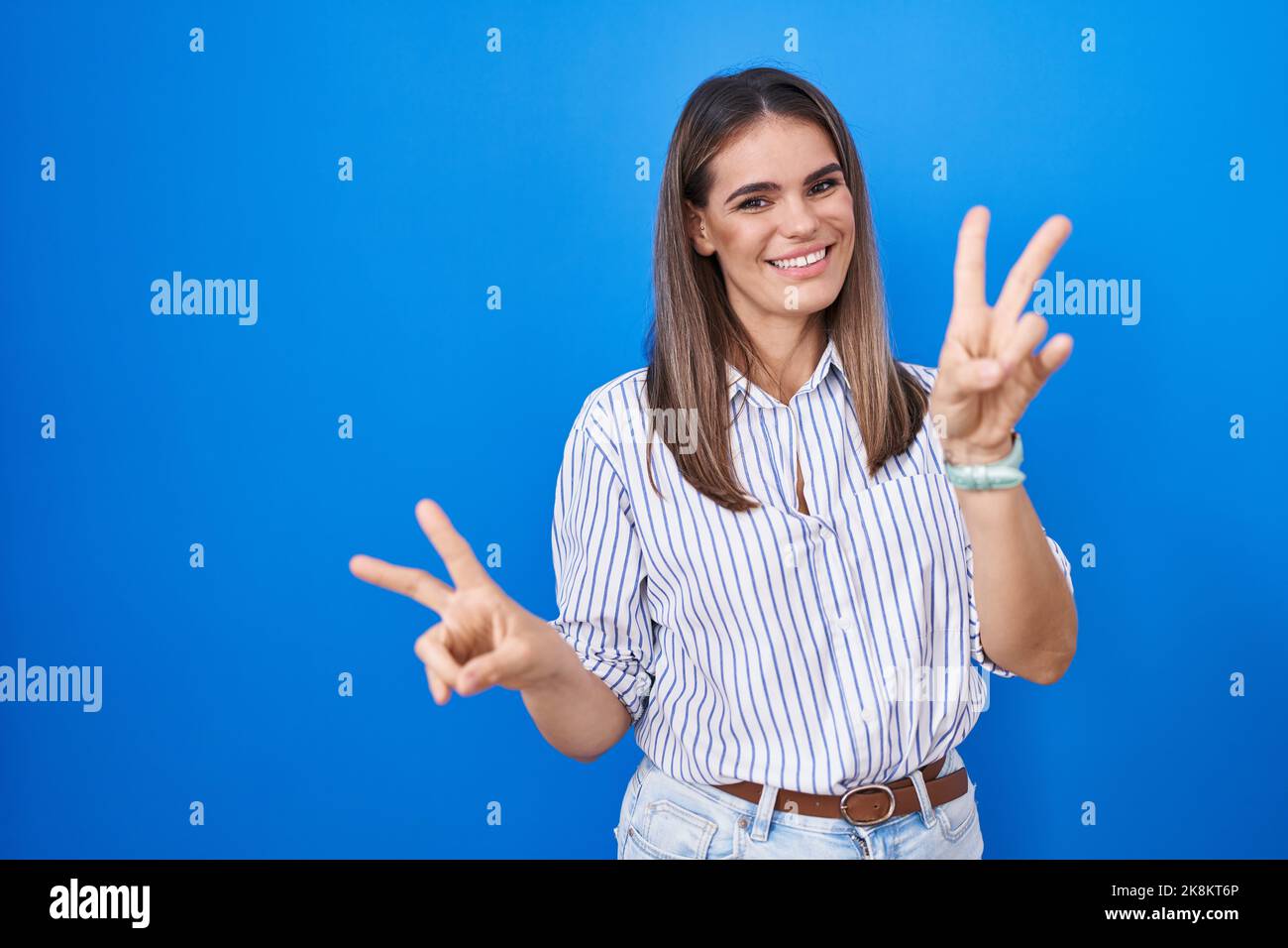 Hispanic young woman standing over blue background smiling looking to ...