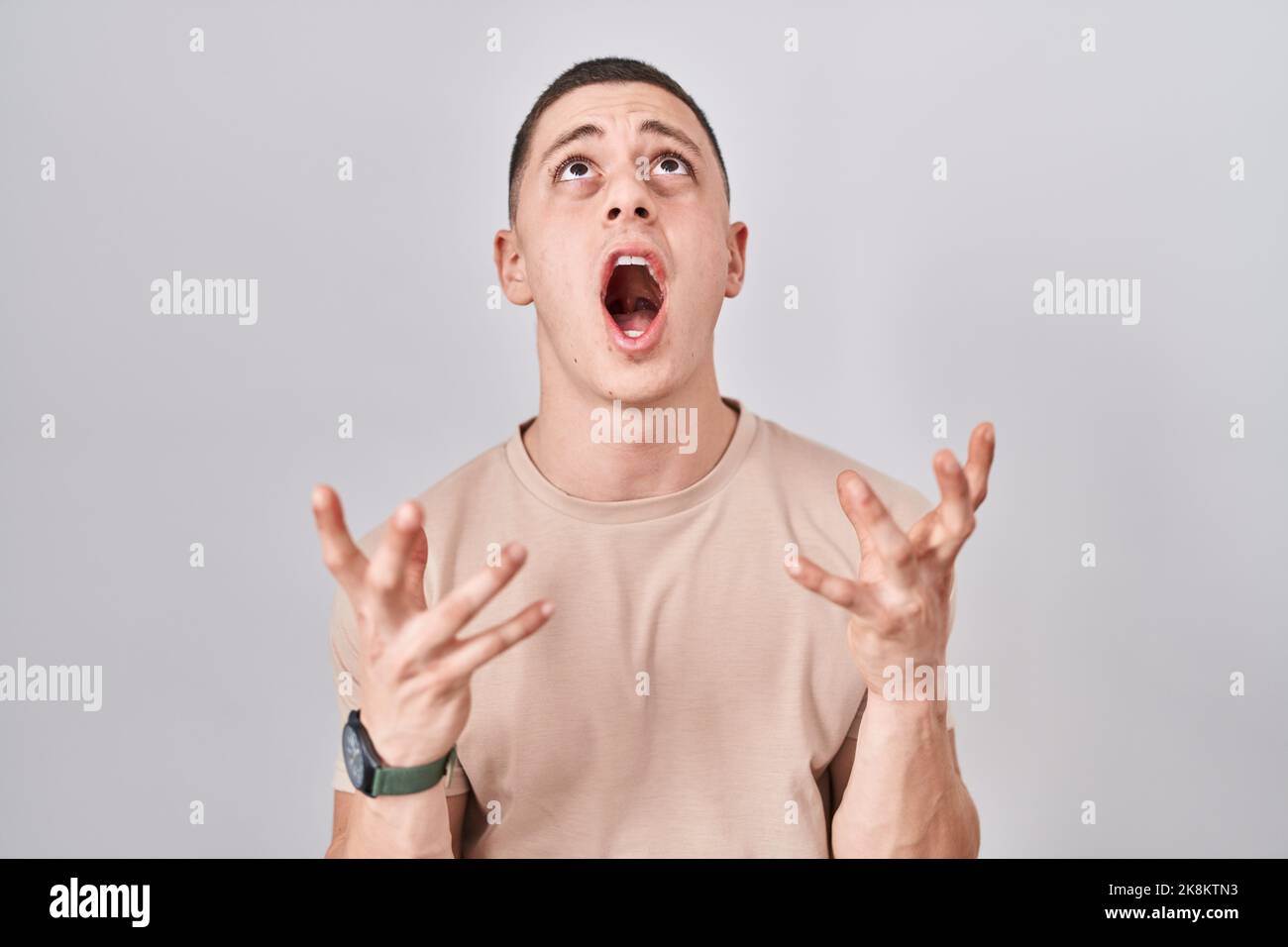 Young man standing over isolated background crazy and mad shouting and ...