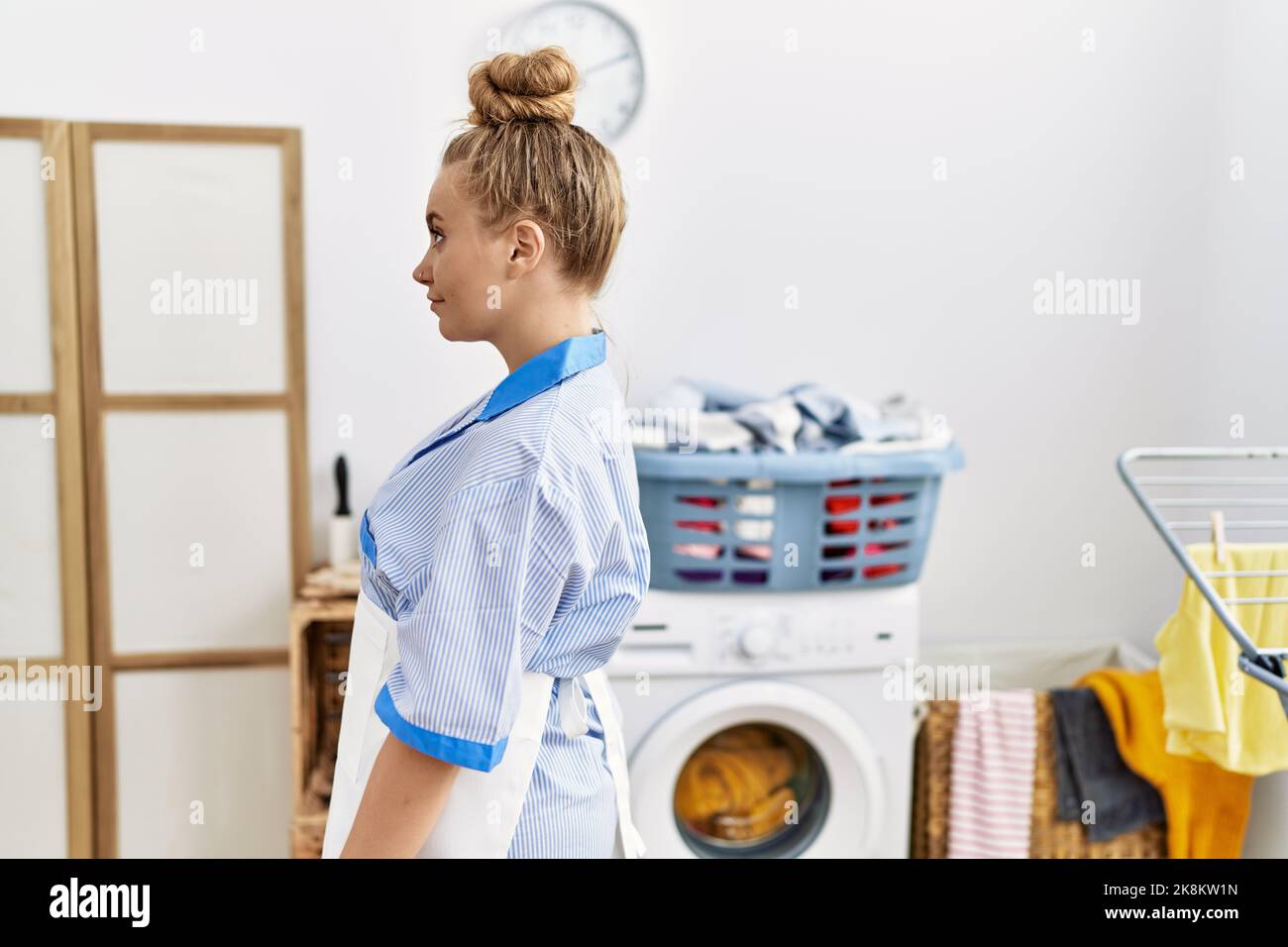 Young caucasian woman wearing cleaner uniform at the laundry room ...