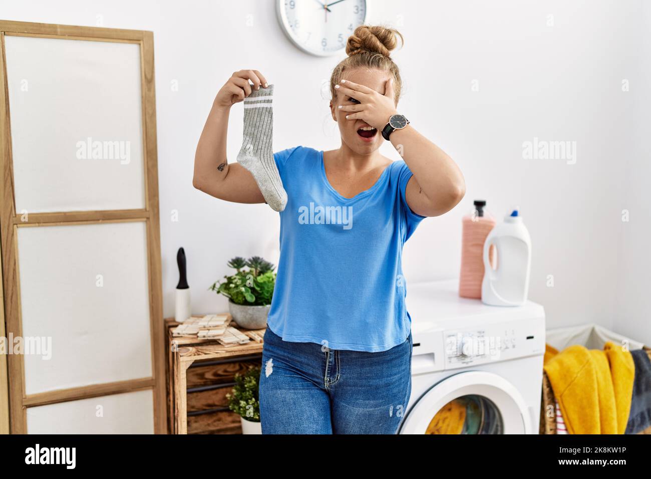 Young caucasian woman holding dirty sock at laundry room peeking in ...