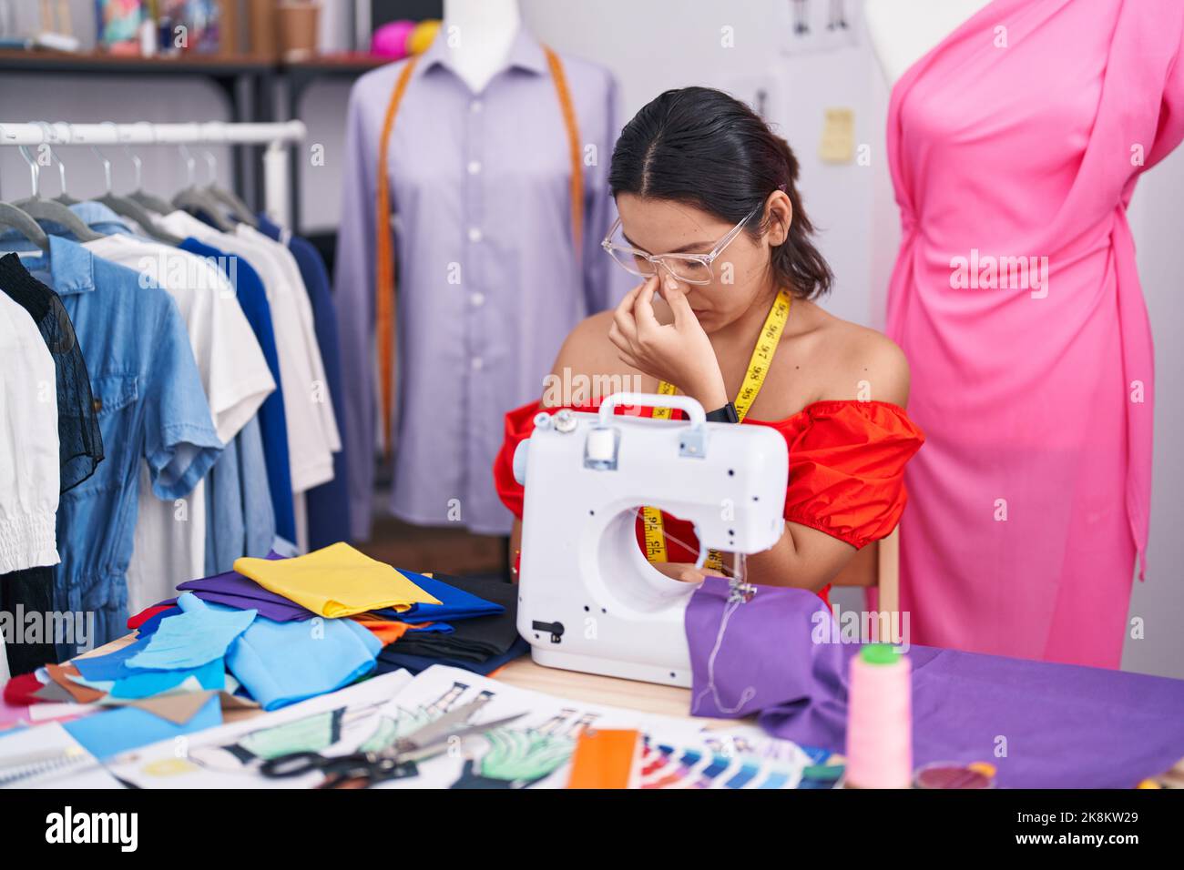 Hispanic young woman dressmaker designer using sewing machine tired ...