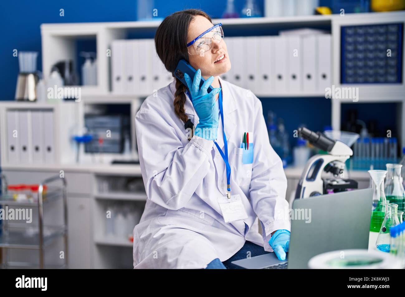 Young woman scientist using laptop talking on the smartphone at ...