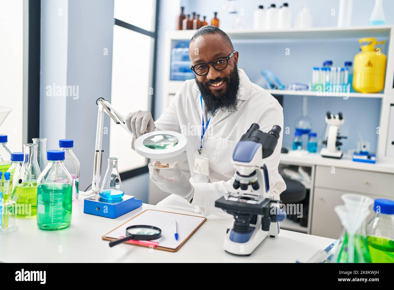 Young african american man wearing scientist uniform using loupe at ...