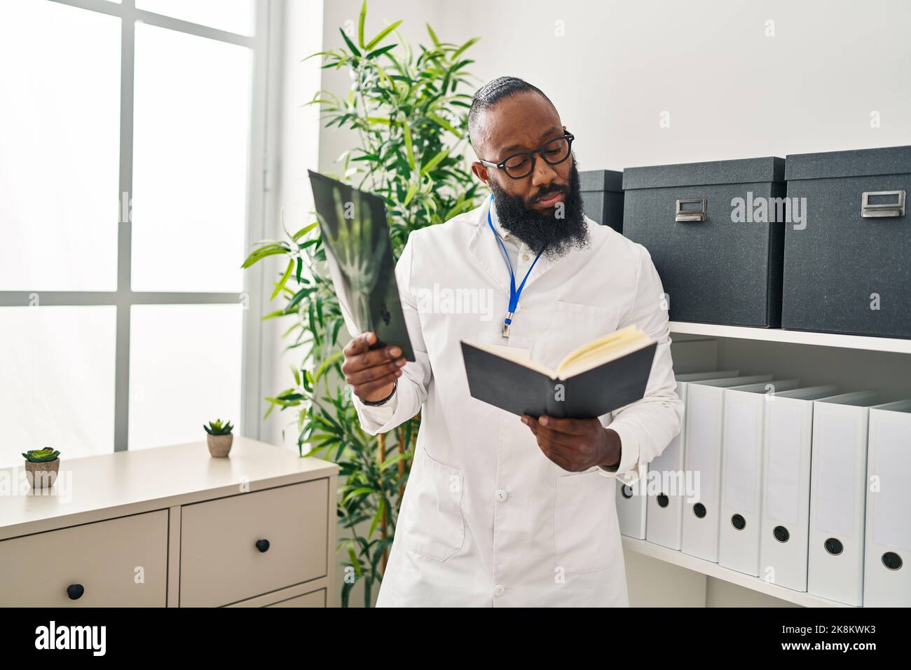 Young african american man wearing doctor uniform reading book looking ...