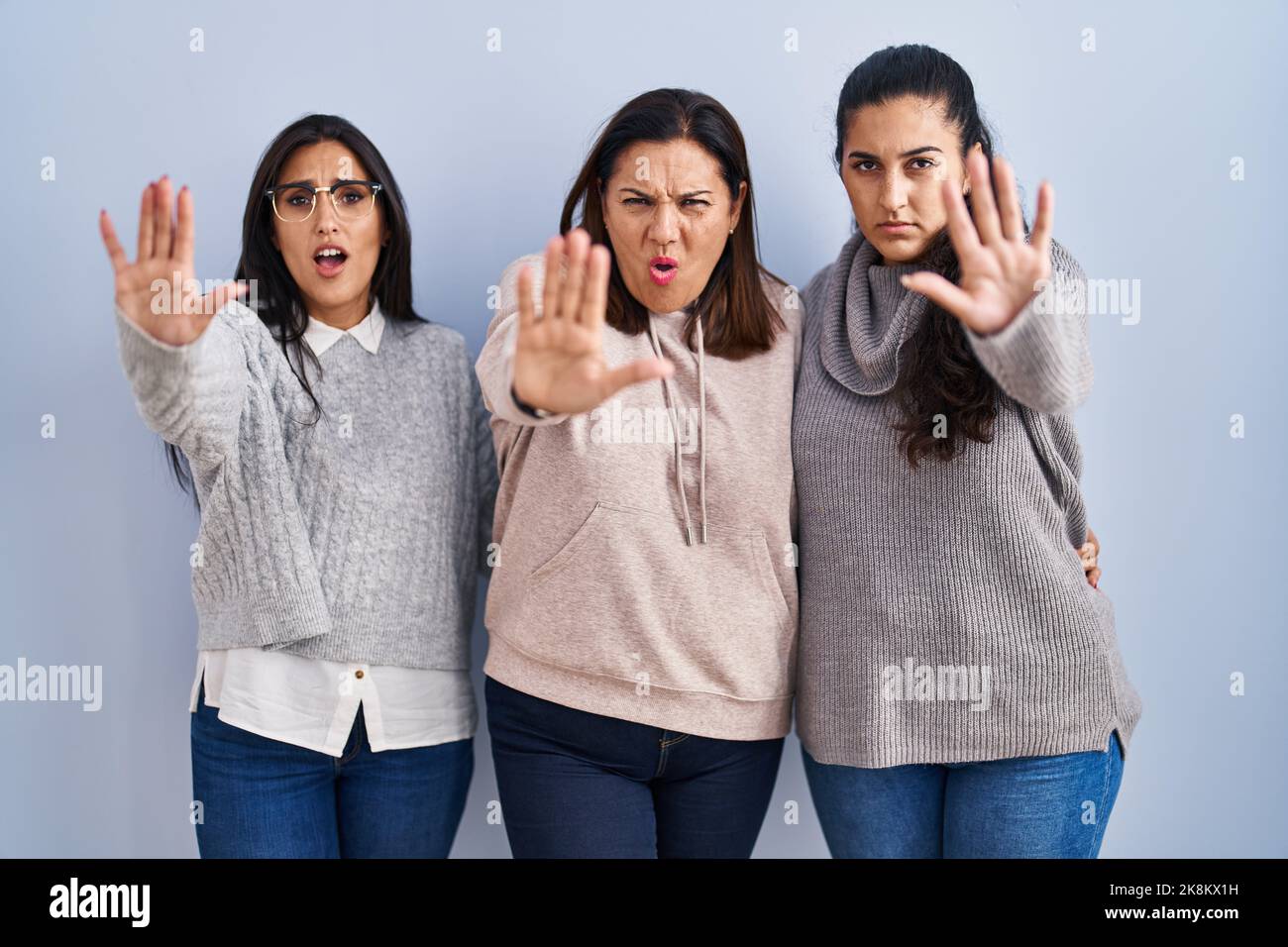 Mother and two daughters standing over blue background doing stop ...