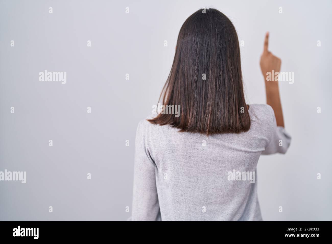 Young hispanic woman standing over white background posing backwards ...