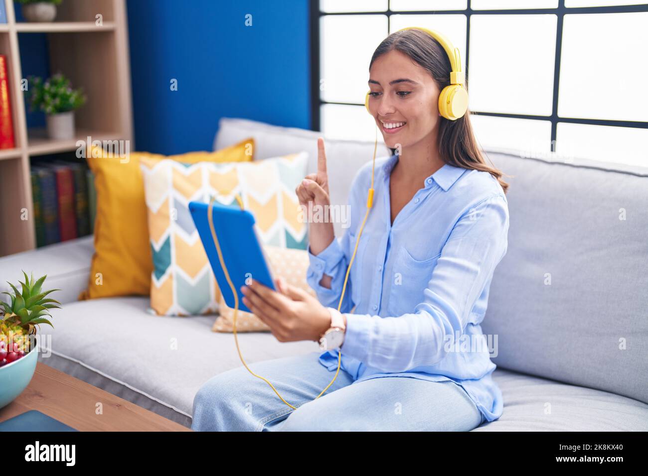Young hispanic woman doing video call with tablet wearing headphones ...