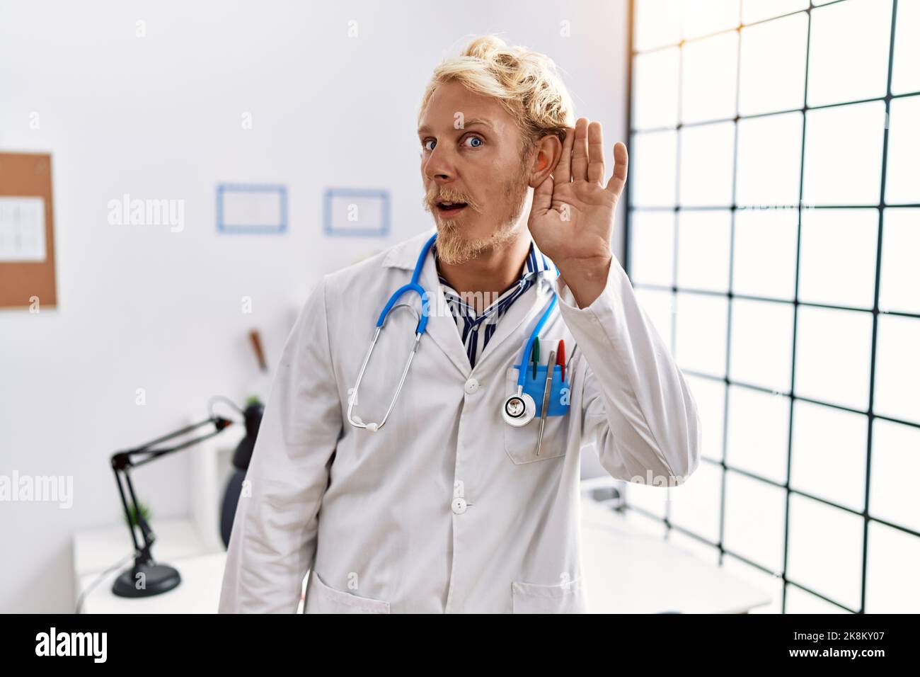 Young blond man wearing doctor uniform and stethoscope at clinic ...