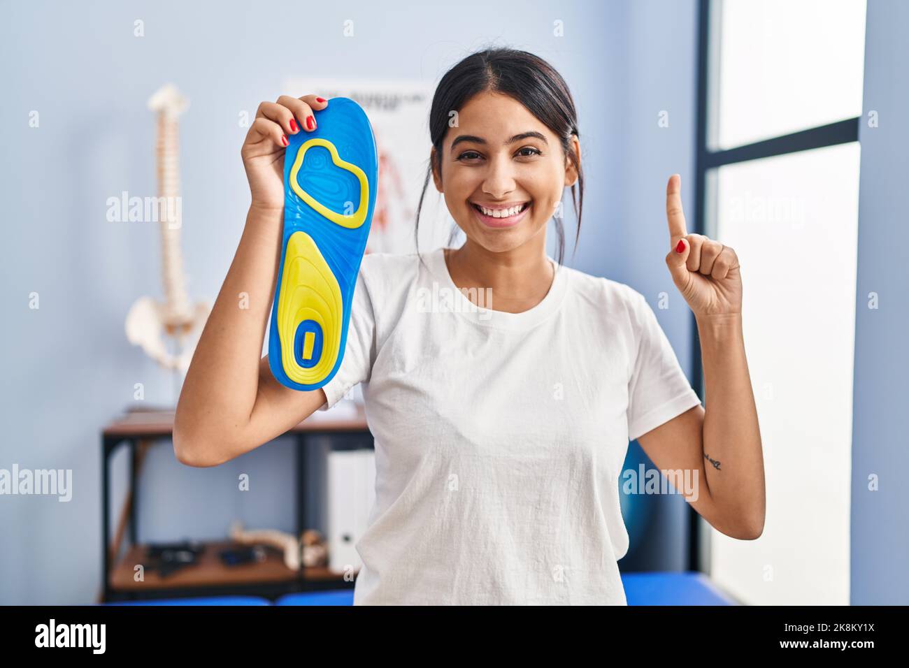 Young hispanic woman holding shoe insole at physiotherapy clinic ...