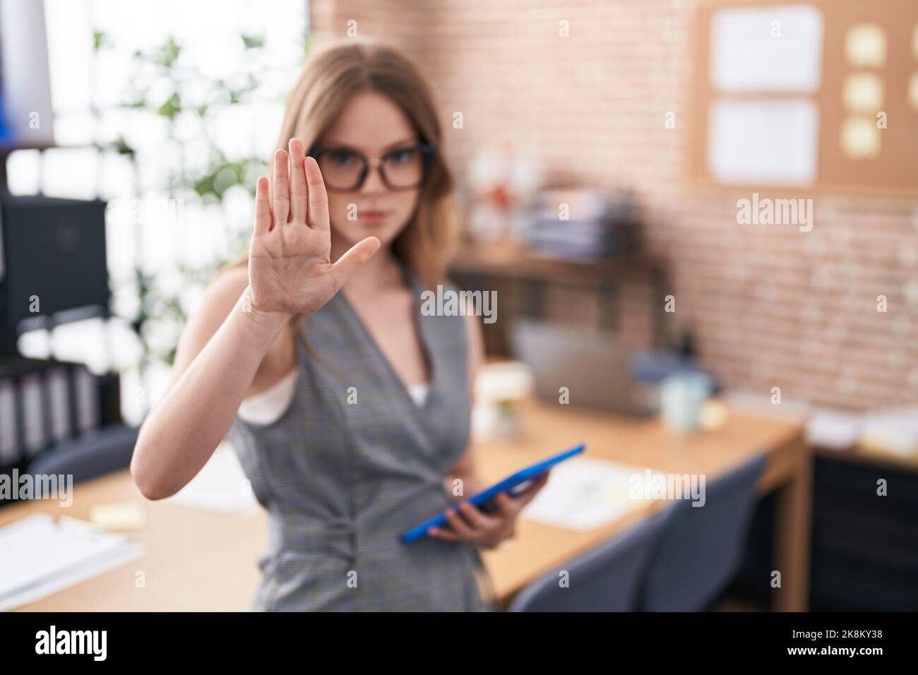 Caucasian woman working at the office wearing glasses doing stop sing ...