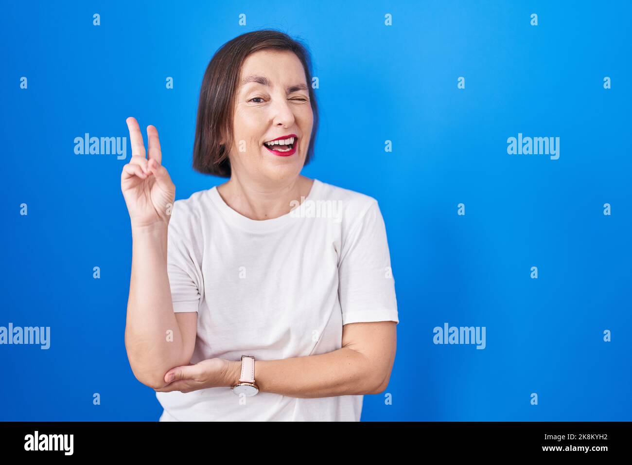 Middle age hispanic woman standing over blue background smiling with ...