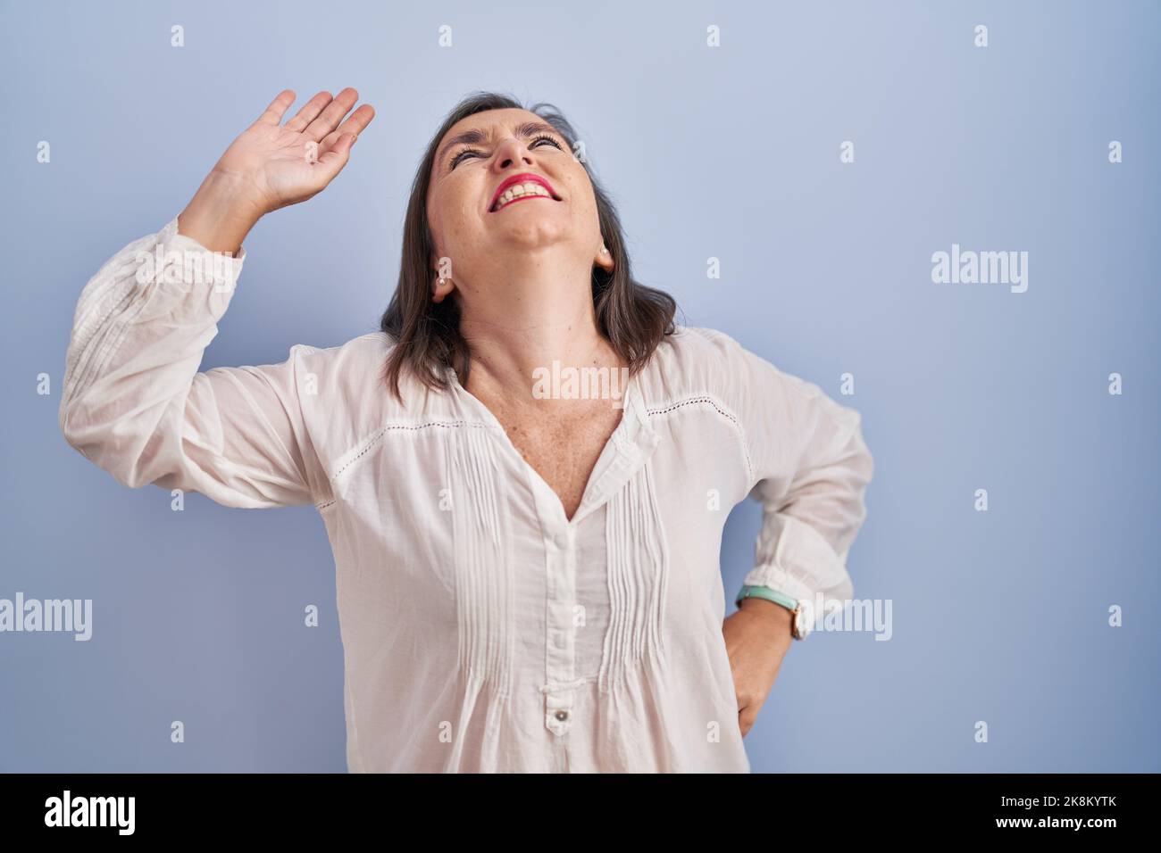 Middle age hispanic woman standing over blue background stretching back ...