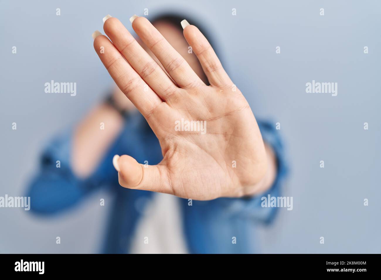 Hispanic woman standing over blue background covering eyes with hands ...