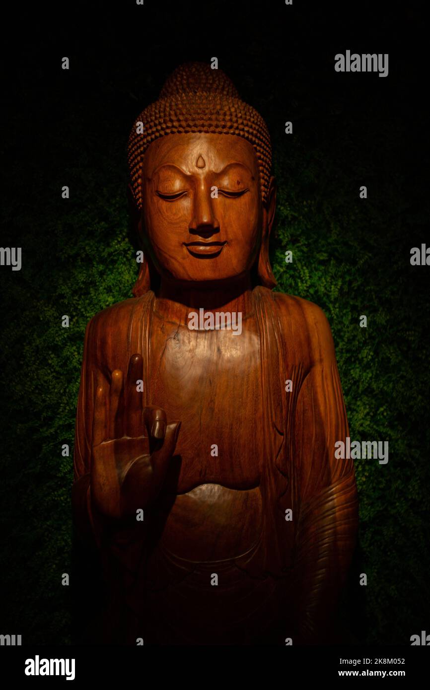 A vertical closeup of an illuminated wooden statue of Buddha Stock ...