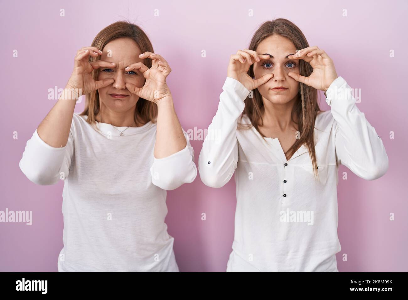 Middle age mother and young daughter standing over pink background ...